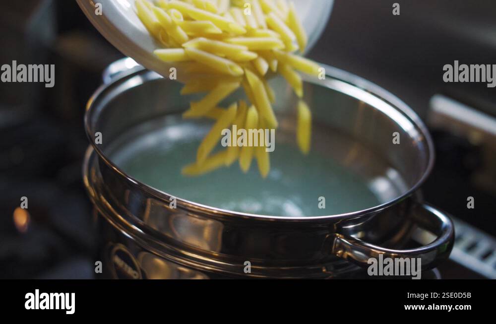 Person Dropping Penne Pasta In A Strainer Pot With Water Over Stove ...