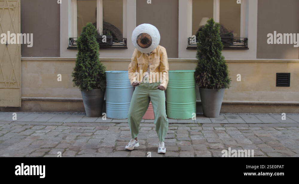 Female dancer with big eye mask on head moving in rhytm at city street ...
