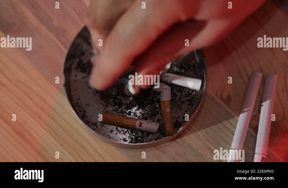 A man in a bar puts out a cigarette in an ashtray and takes a new ...