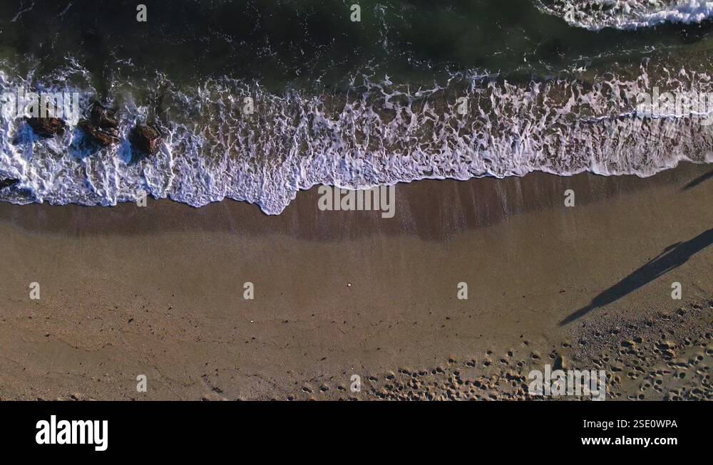 Aerial view of beach waves with a couple of people passing by Stock ...