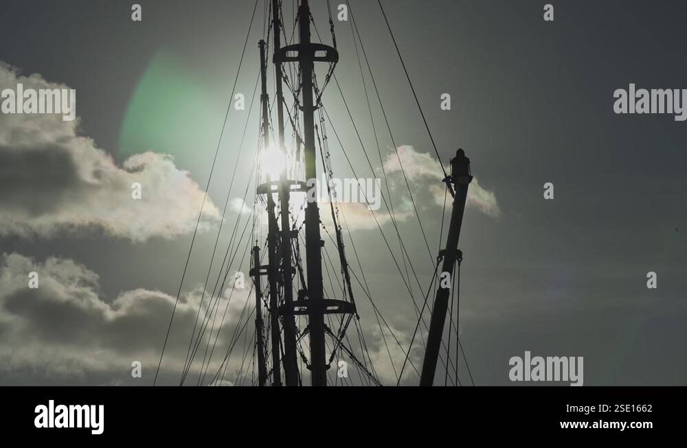 Silhouette of Mast and ropes of a ship, blocking the Sun and cloudy sky ...