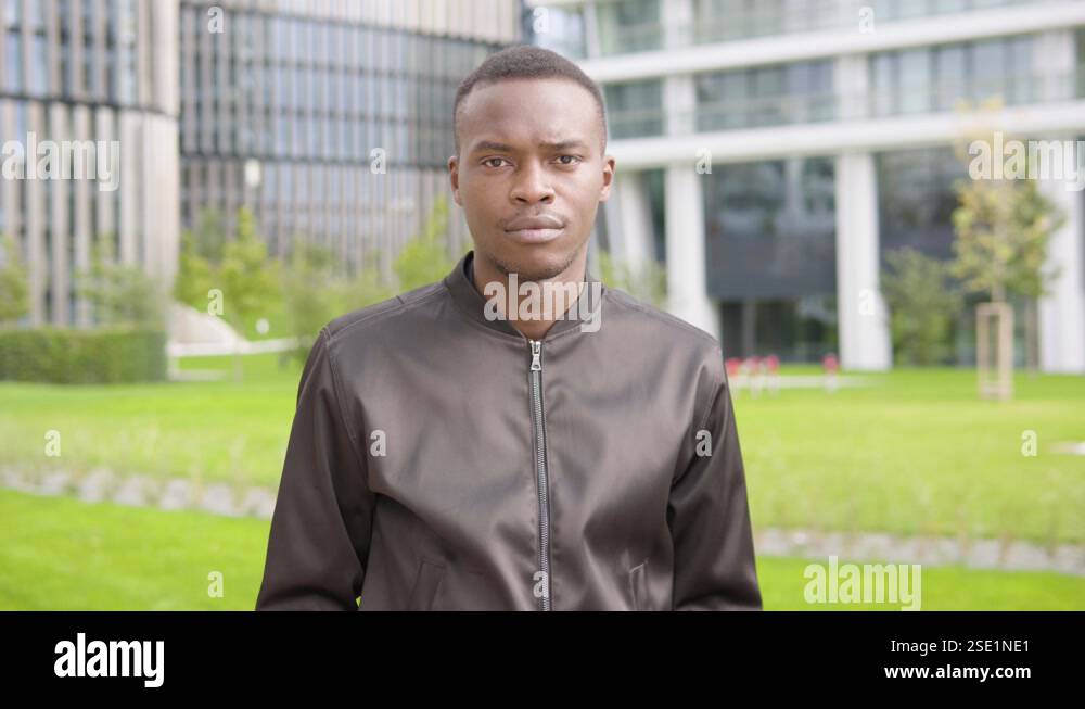 A young black man nods at the camera with a smile - office buildings in ...