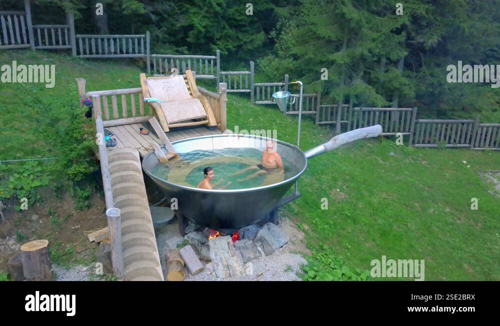 A couple getting in a pot shape hot tub with a woodfire burning Stock ...