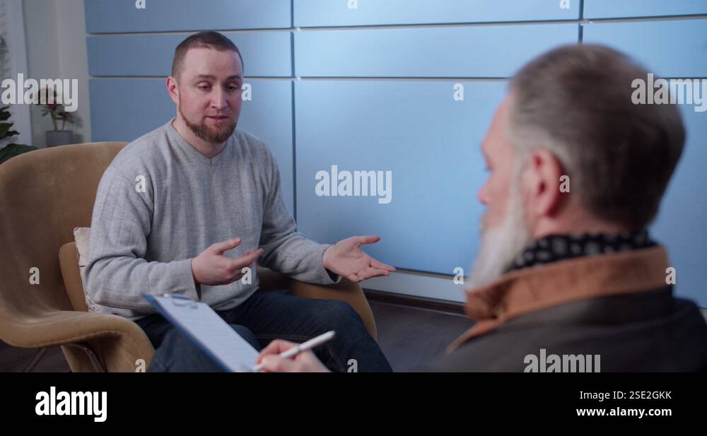 Professional gray-haired male psychologist listens to a patient and ...