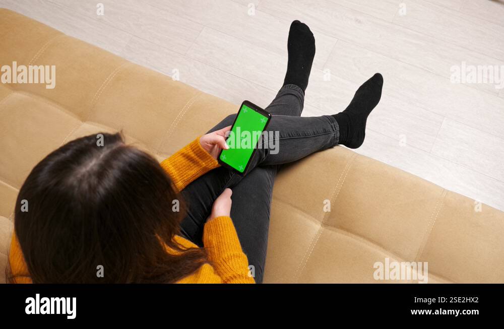 Brunette in jeans sits on sofa with green screen smartphone Stock Video ...