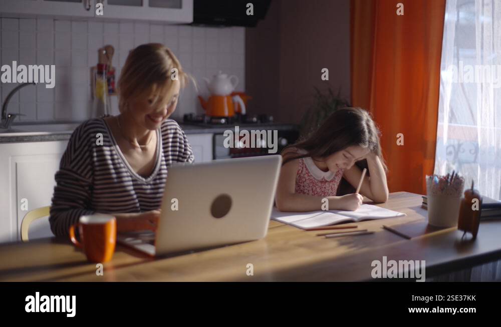 Girl is doing her lessons while mom is working on the computer in the ...