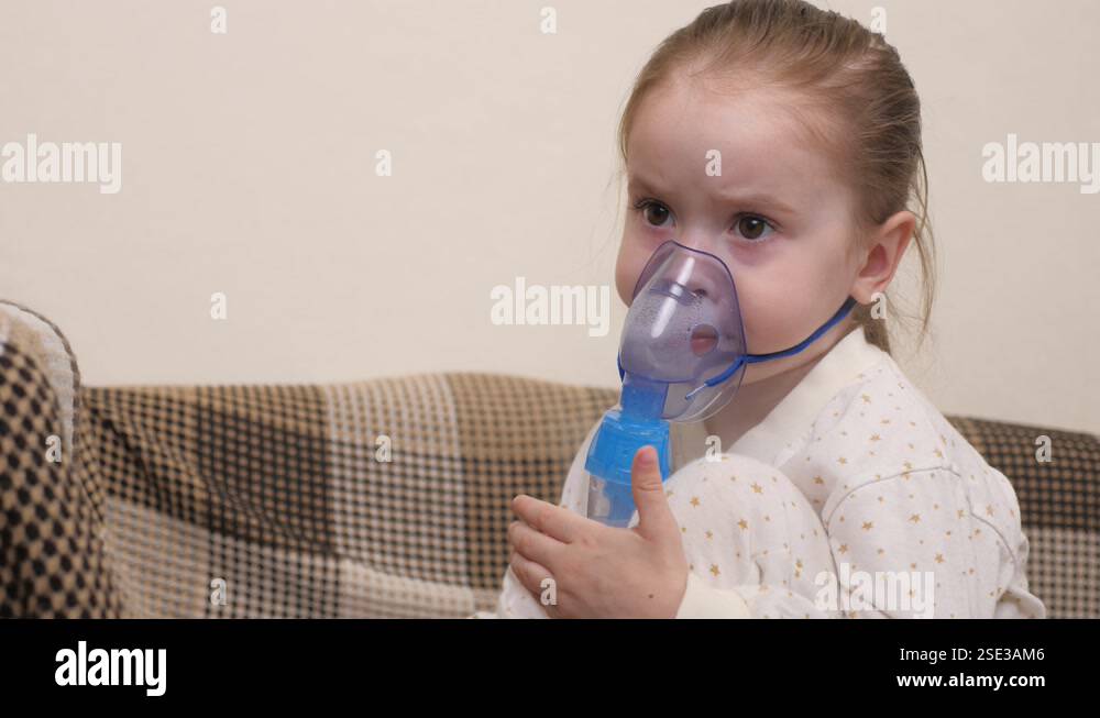 A cute baby in a mask is breathing through an inhaler. Home inhalation ...