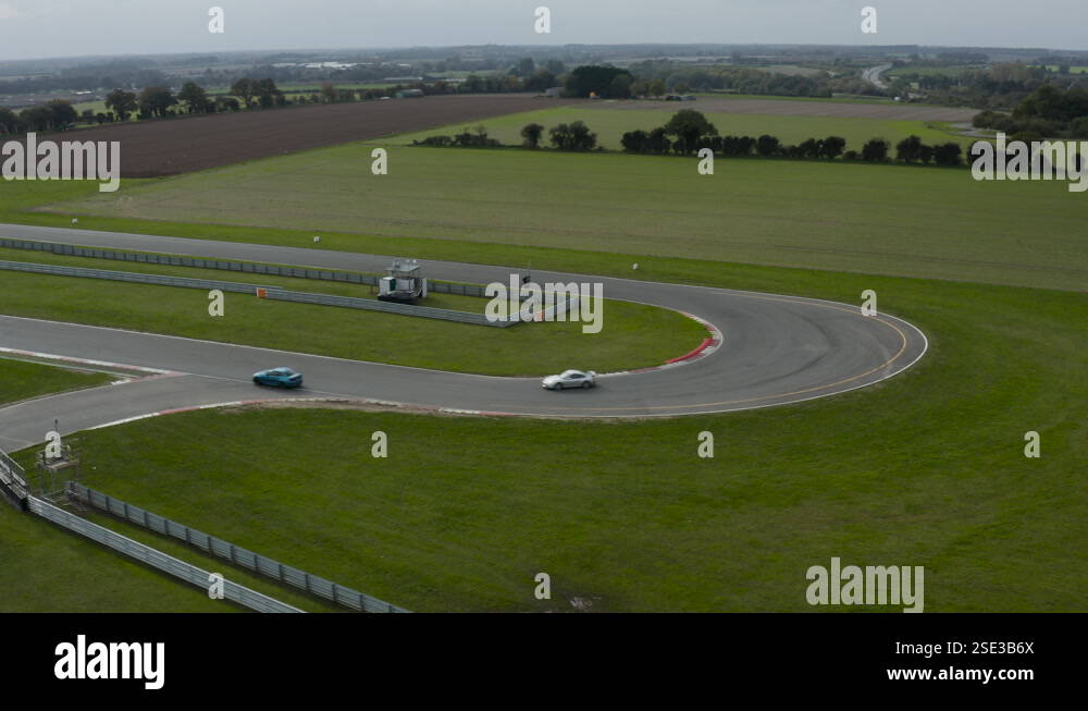 Two cars racing around a track in the countryside surrounded by green ...