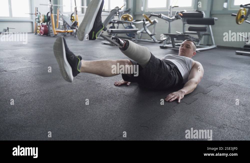 Athlete with prosthetic leg doing ab exercises on the gym floor. Slow ...