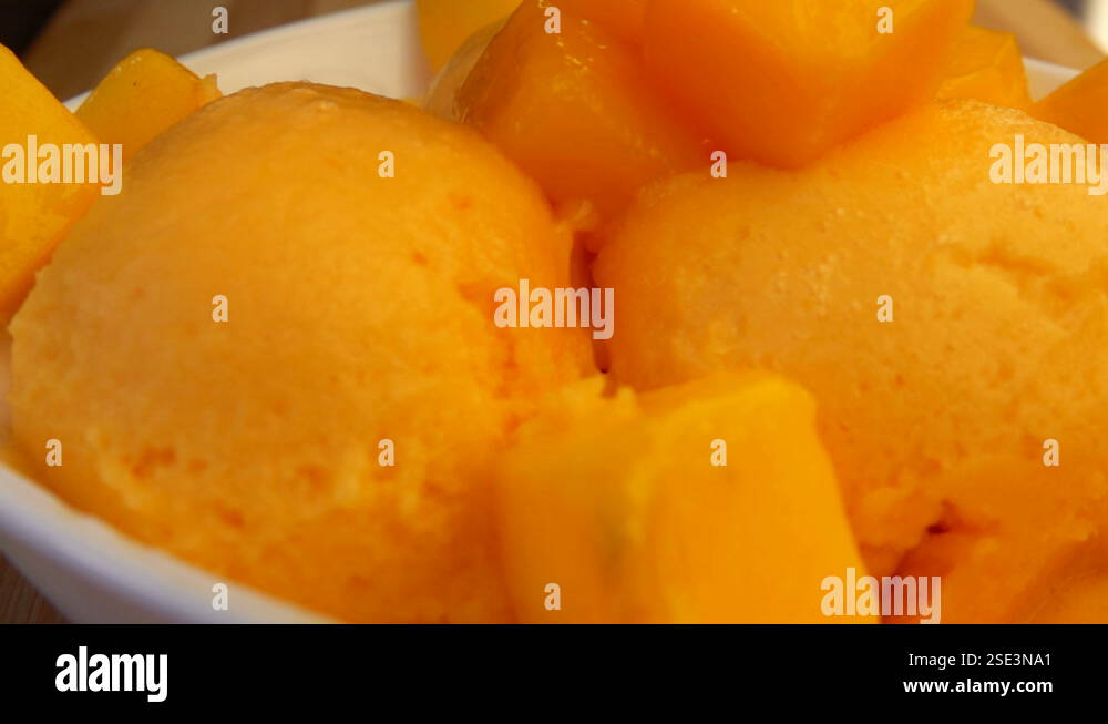 Cubes of fresh mango are falling in the bowl full of frozen mango ice ...
