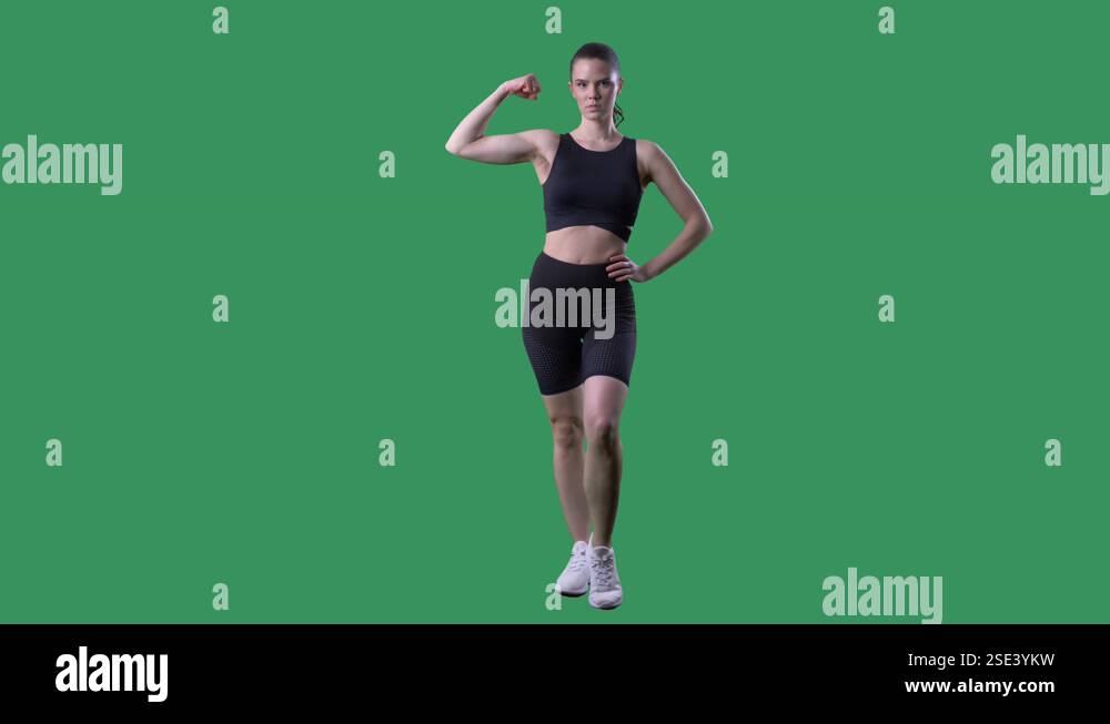 Proud fitness woman flexing biceps muscles showing. Full body on green ...