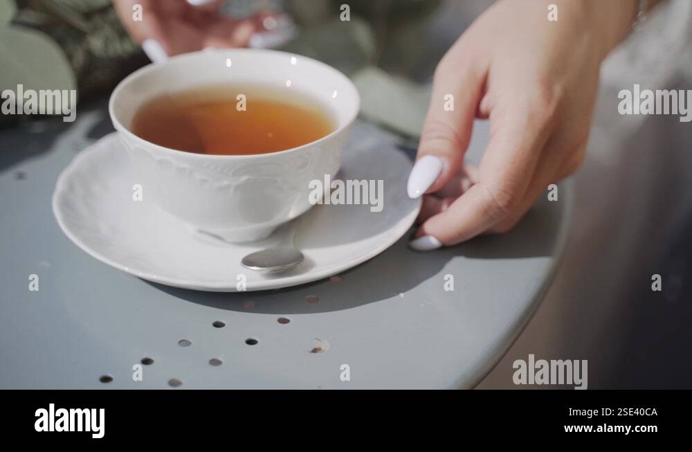 White cup with tea stands on table in fresh air. Female hands take a ...