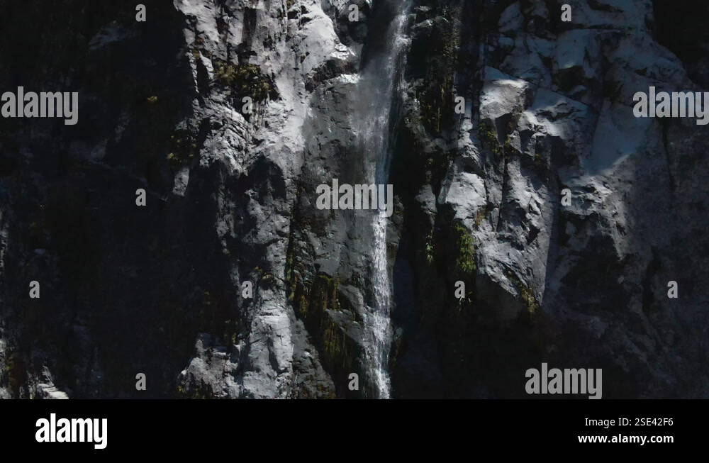 Fast flowing waterfall down a sheer rocky mountain cliff in Fiordland ...