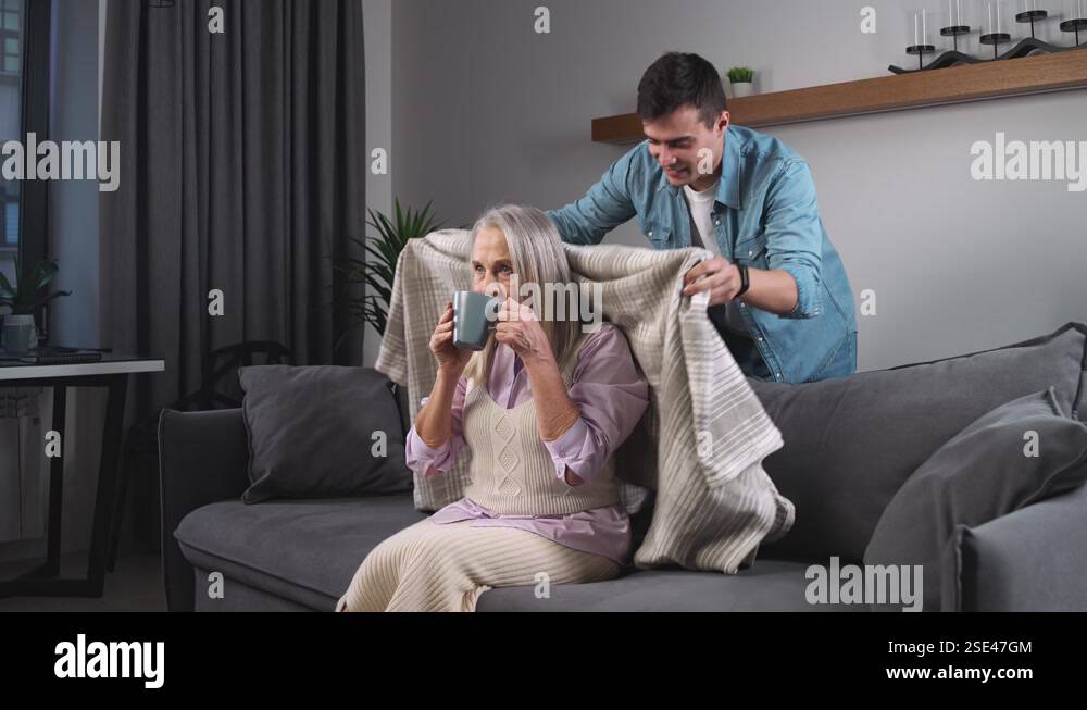 Young man covers his grandmother with a blanket, taking care of their ...