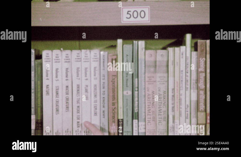 1960s: Library. Books on shelves. Woman points to book spines Stock ...