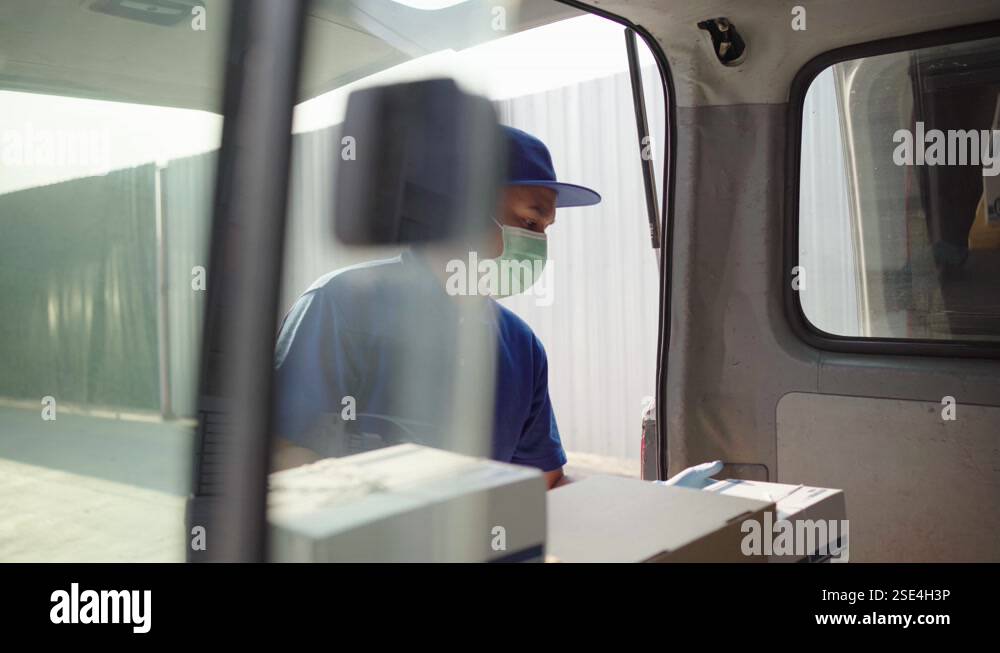 Blue delivery man arranges parcels from the trunk of the car and ...