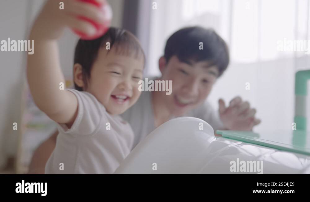 Toothy smiling baby girl in father's hands catching ball on playhouse ...