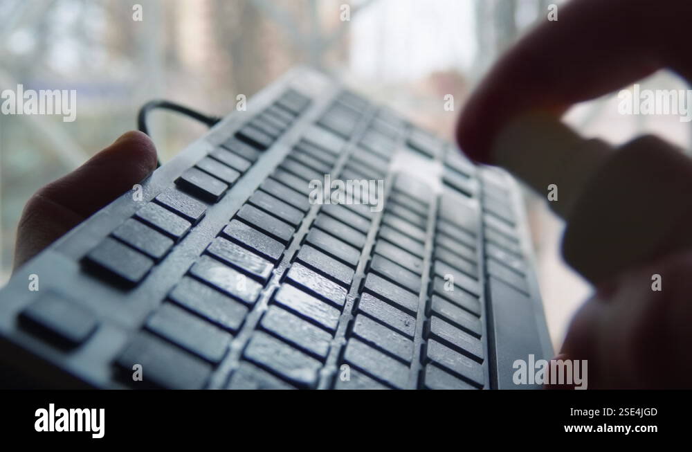 Disinfecting a computer keyboard with an antibacterial spray during a ...