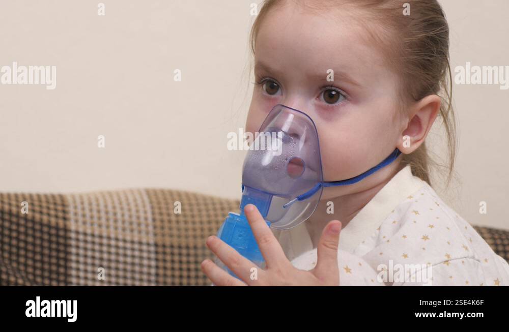 A cute baby in a mask is breathing through an inhaler. Home inhalation ...