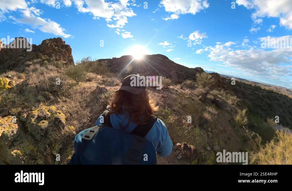 Sun flares burst over red-haired hiker crests a hill in a rocky ...