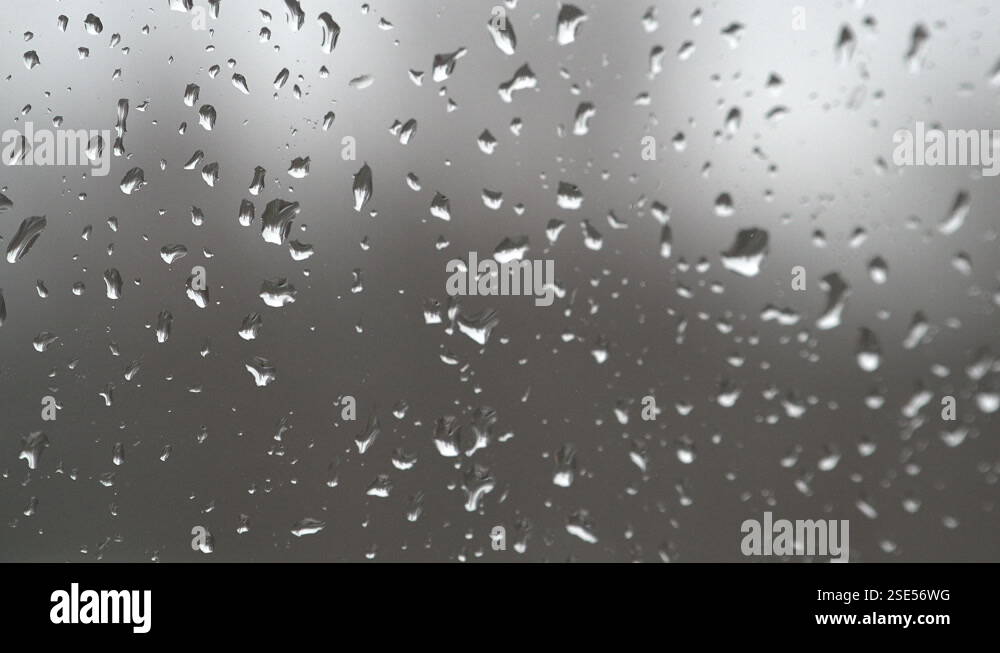 Rain drops land on a window and trickle down the glass during a rain ...