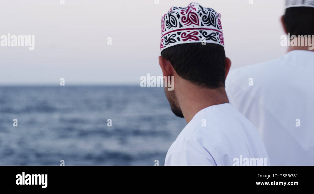 Two men wearing kuma caps in front of the ocean, Muscat, Oman, medium ...