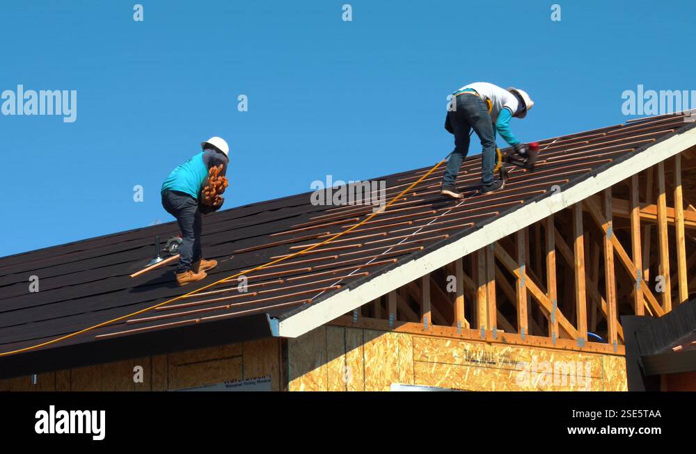 Two workers nailing wood slats for installation of ceramic roofing ...