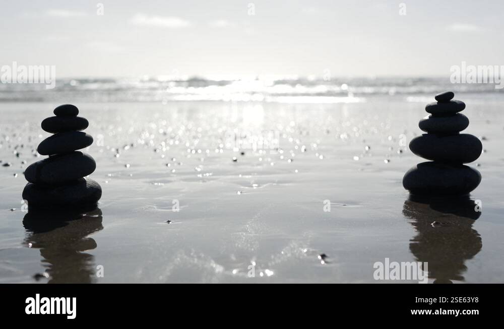 Rock balancing on ocean beach, stones stacking by sea water waves ...