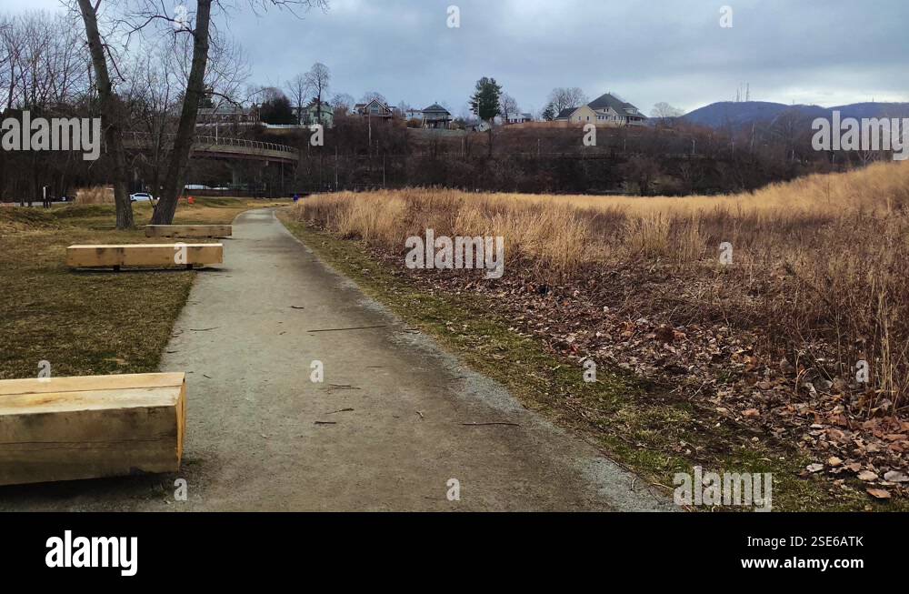 A walking path with benches in a public green space next to a small ...