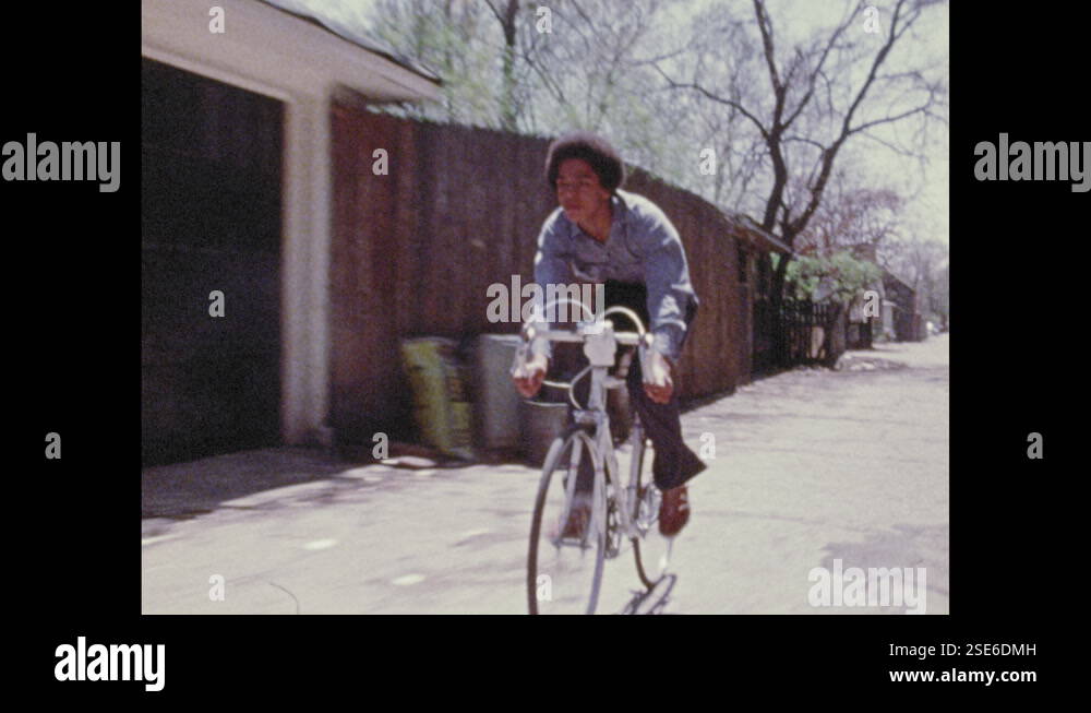 1970s: Boy riding bike in alley. Stop sign, zoom out to intersection ...