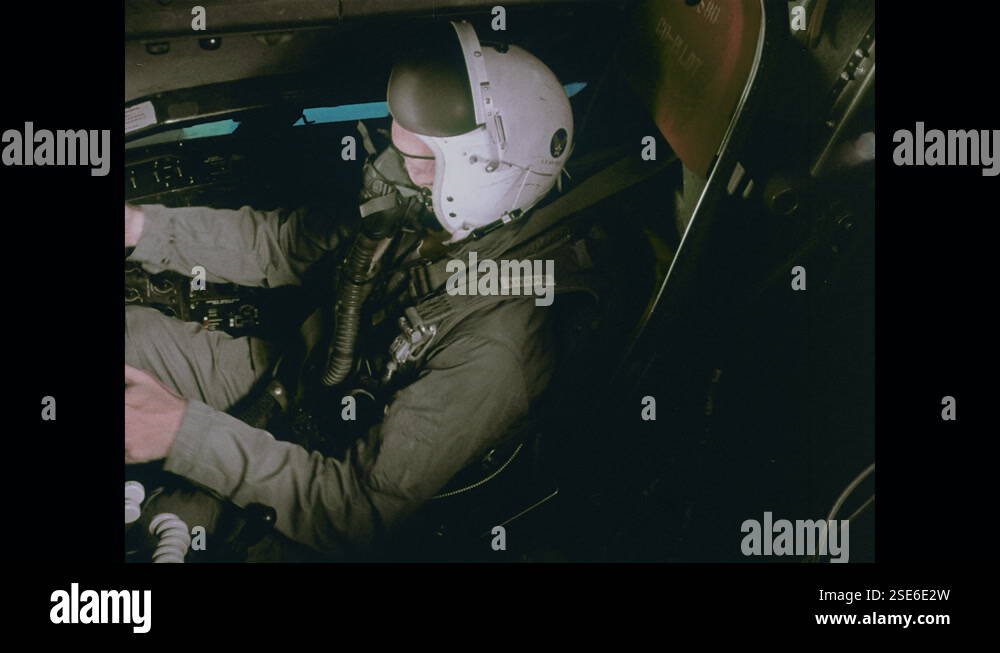 1960s: Man in cockpit puts hands on yoke. Man wearing gas mask nods ...