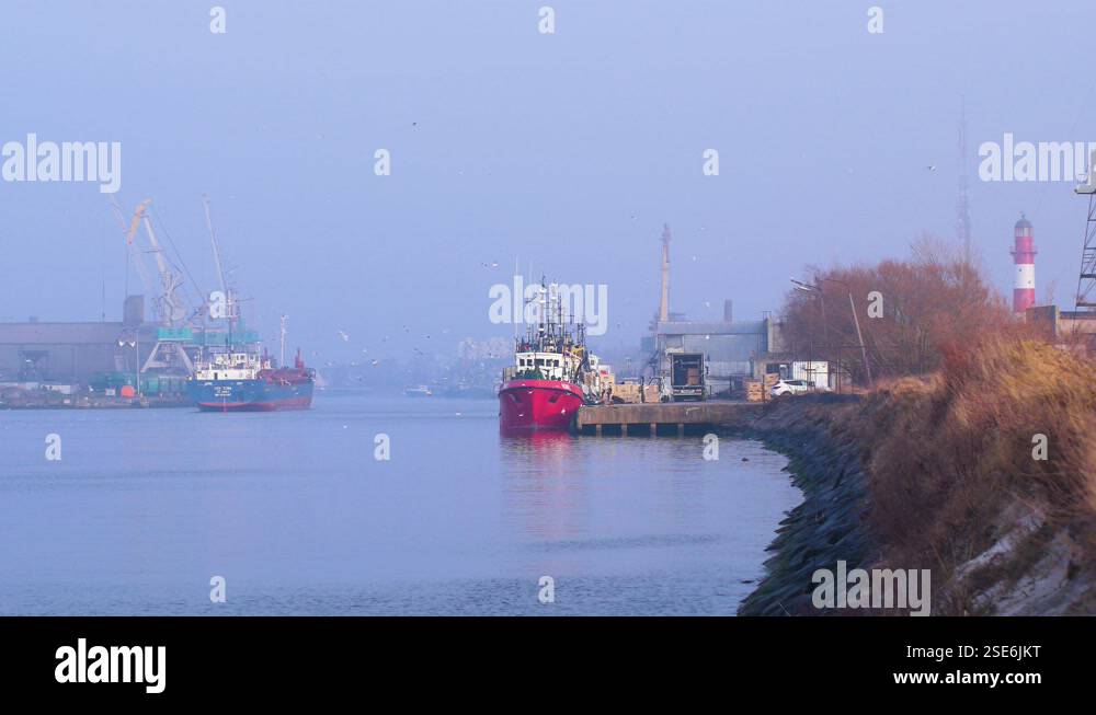 Large blue cargo ship and fishing vessels at Port of Liepaja in foggy ...