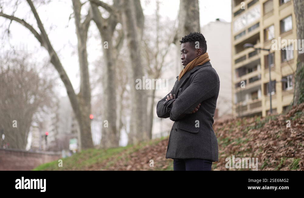 Black man arms crossed standing outside at park thinking wearing winter ...
