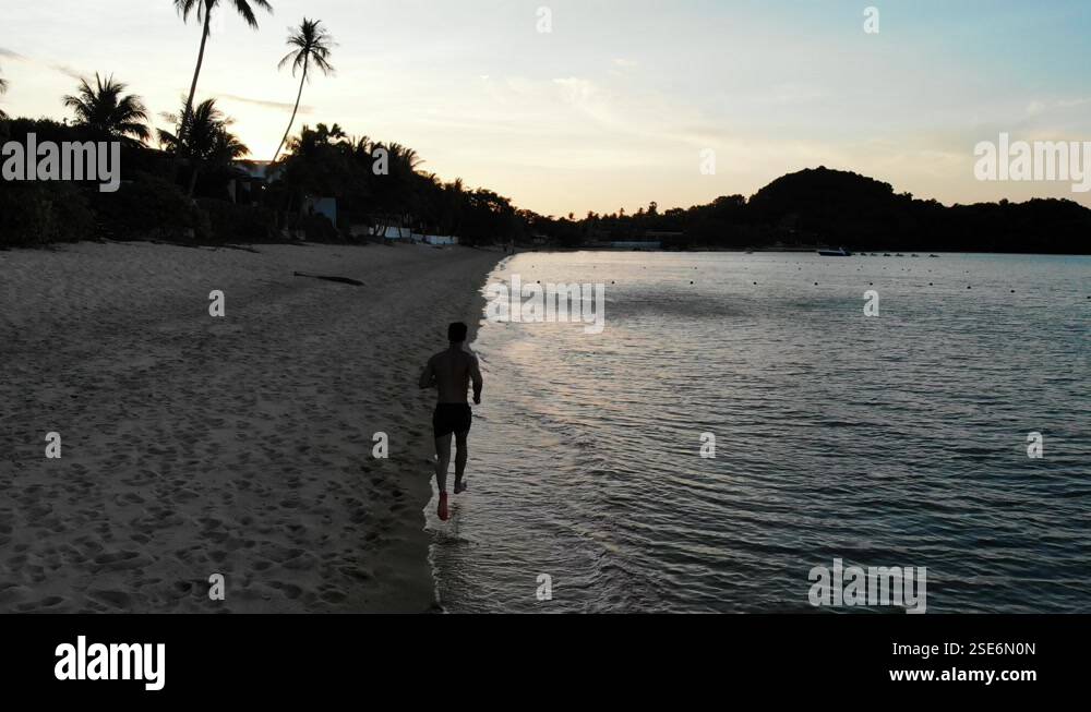 Following a young fast man running on the sand beach in Thailand ...