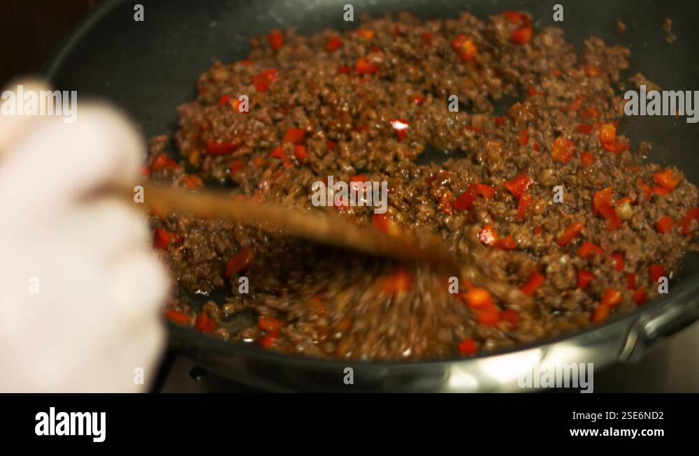 Mixing juicy ground beef and other ingredients cooking on a frying pan ...