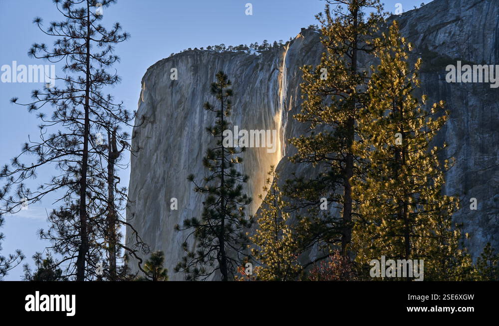 sun sets on yosemite waterfall as mist shines orange in fading sunlight ...