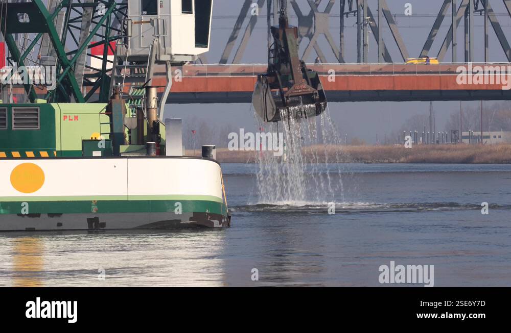 Rotating crane on top of a dredging ship in front of a bridge clearing ...