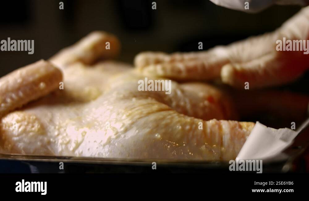Female chef spreading melted butter over a big spatchcocked raw chicken ...