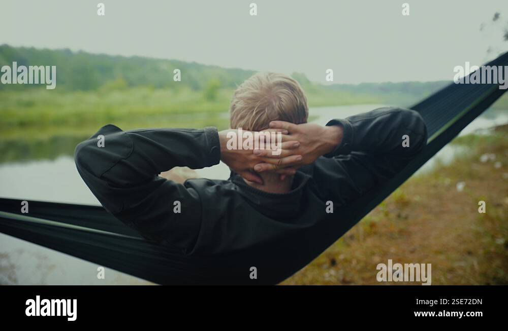 A blond man with hands behind his head breathing with river smell in a ...