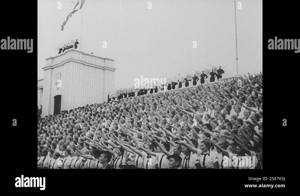 1930s: Crowd at Nazi rally give salute. Nazi flag. Adolph Hitler rides ...