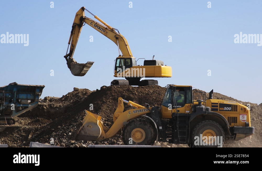 Stationary digger with wheeled digger driving past mound of earth ...