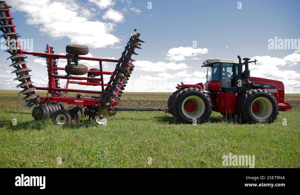 Tractor with harrow system plowing ground on cultivated farm field ...