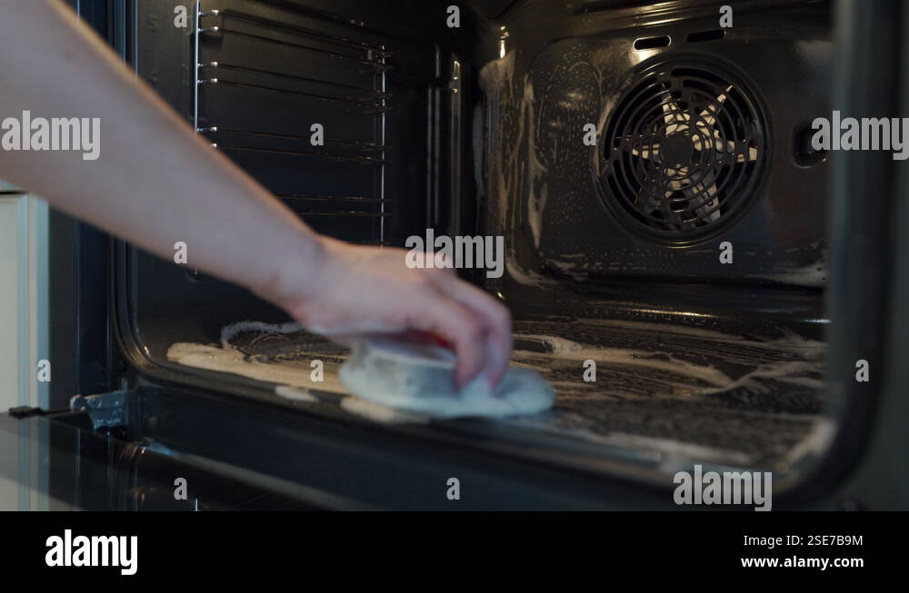 Housewife doing household chores woman cleaning oven with a rag in the ...