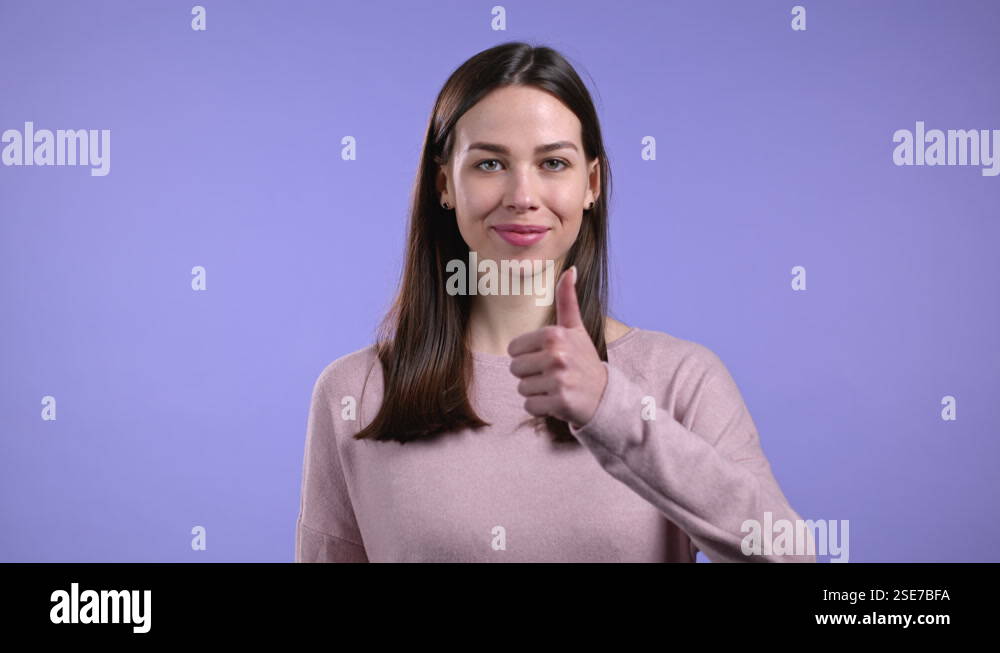 Pretty woman showing thumb up like sign over violet studio background ...