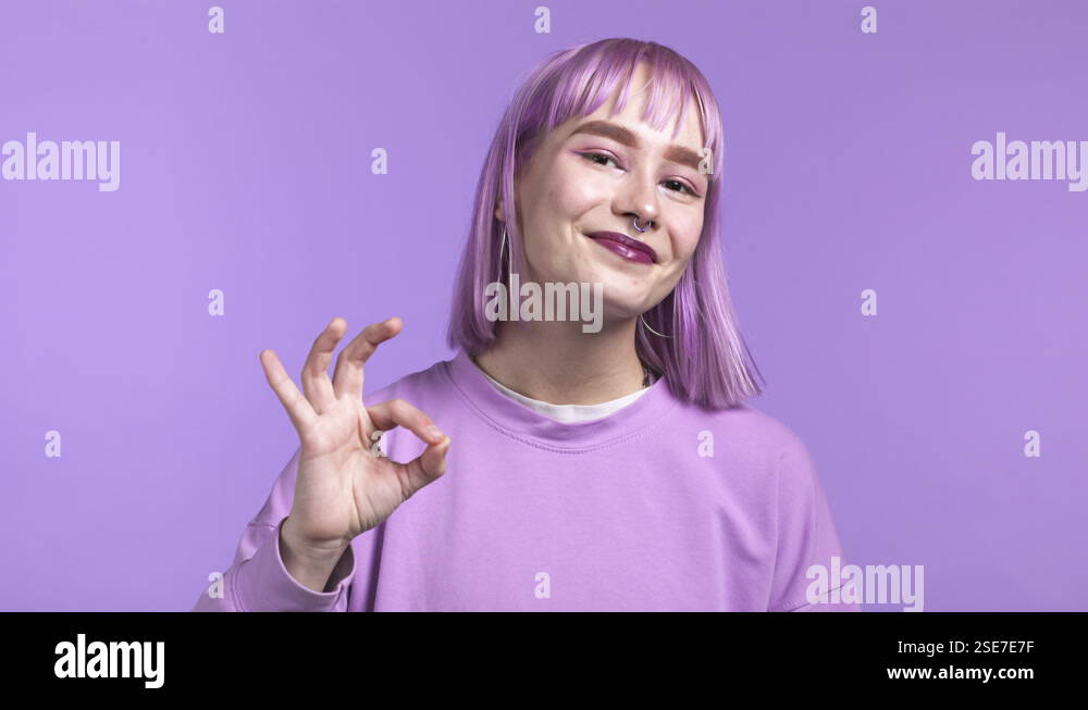 Young woman showing Ok, like sign over violet studio background ...
