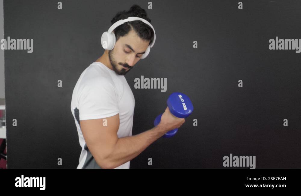 Man lifting blue hand weights with both hands indoors with dark ...