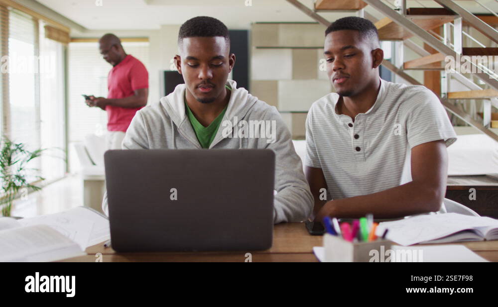 Two african american teenage twin brothers using a laptop and talking ...