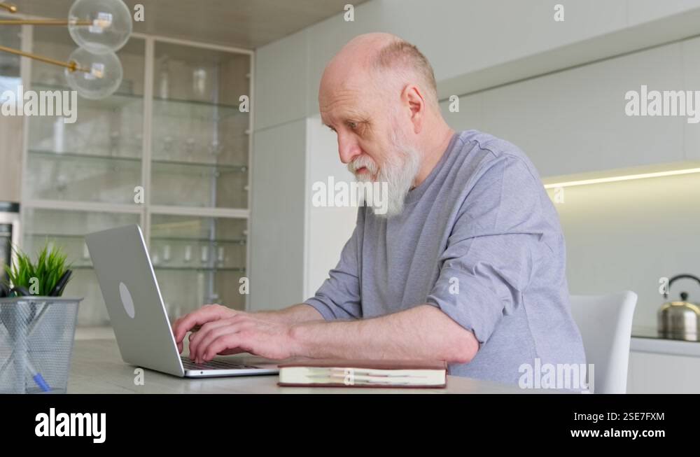 Cute elderly old man works at home behind laptop. Retired grandfather ...