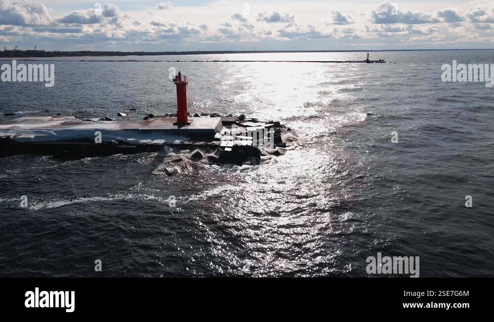 Aerial dolly in: Waves hitting pier and lighthouse in winter with snow ...
