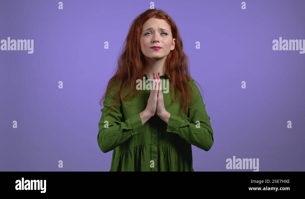 Pretty woman praying over violet background. Girl with red long hair ...